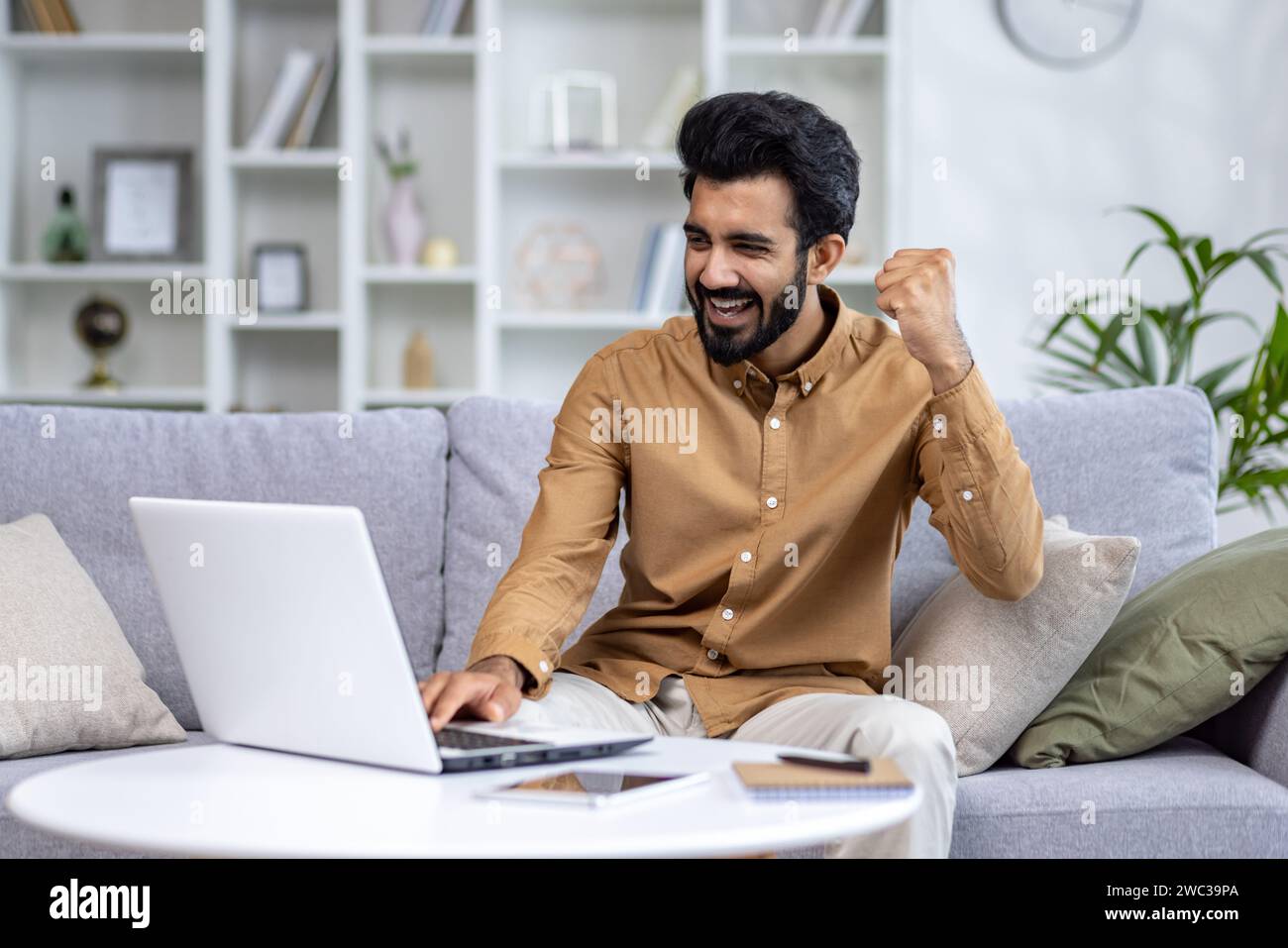 Joyful man celebrating success with a fist pump while working on a ...