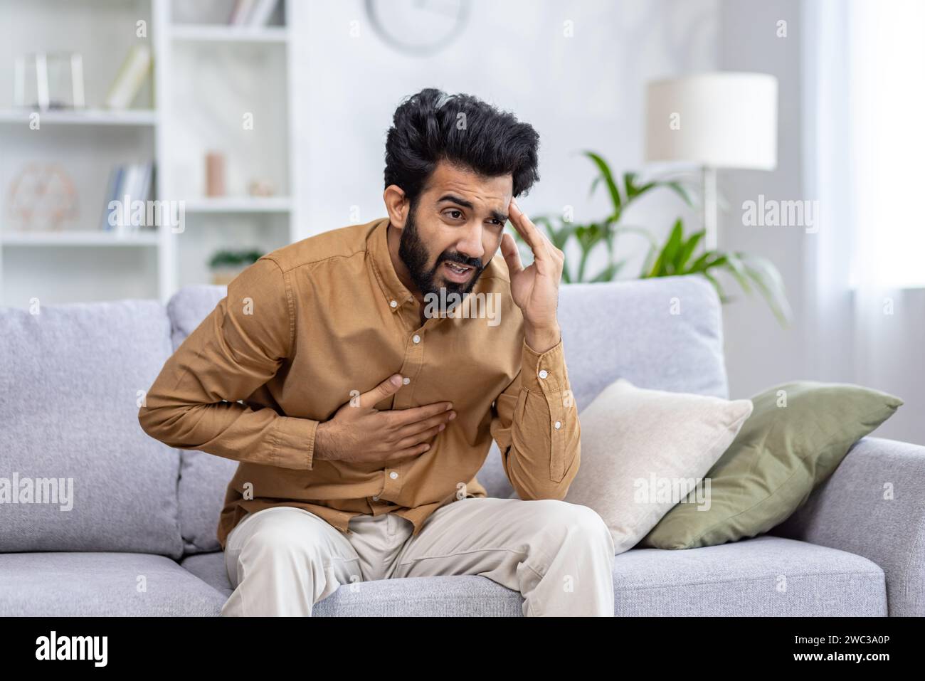 Worried man sitting on sofa, hand on head, expressing stress or ...