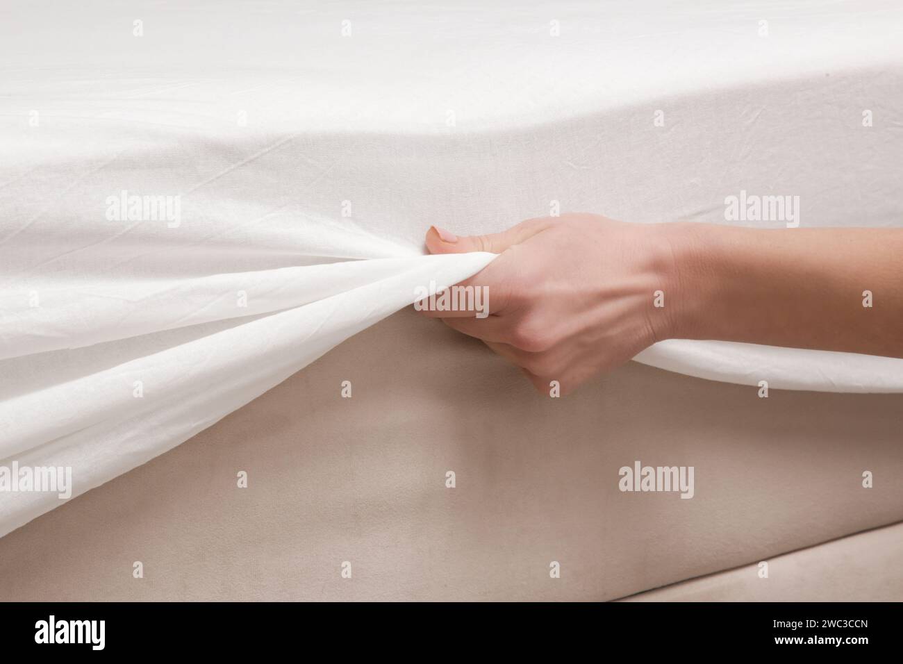 Changing bed sheets. Woman is putting on a fitted white cotton sheet on a mattress while making ...