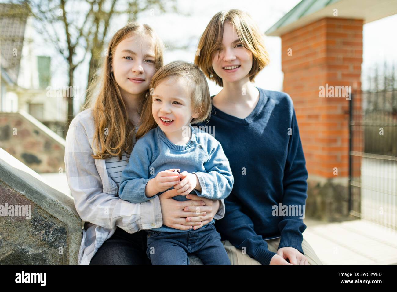 Cute big sisters cuddling with their toddler brother. Adorable teenage ...
