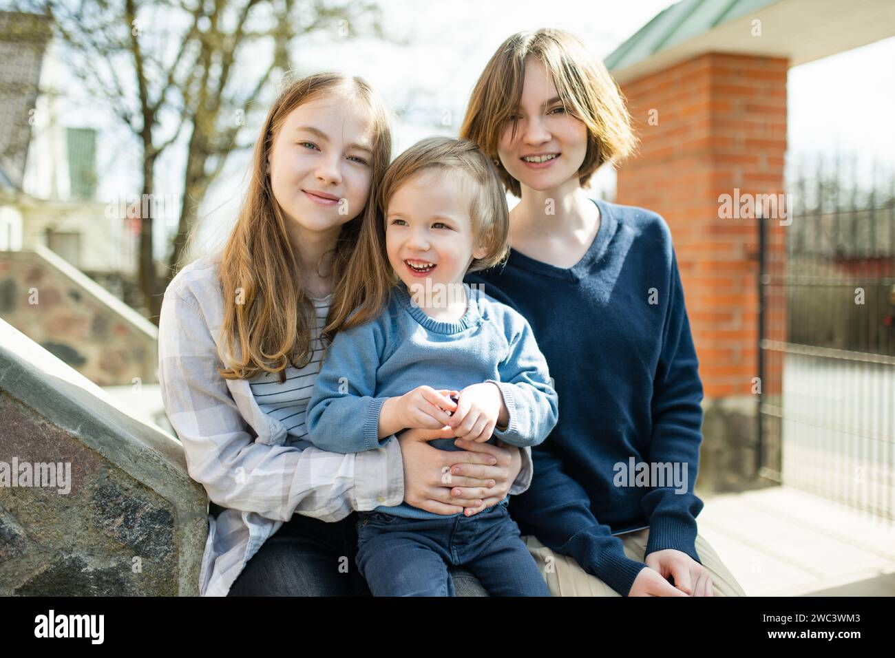 Cute big sisters cuddling with their toddler brother. Adorable teenage ...