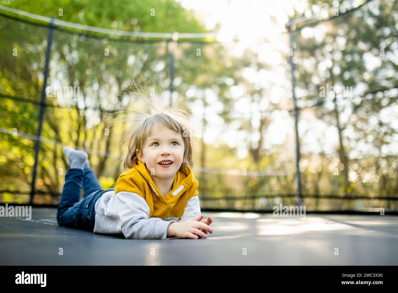 Cute little boy jumping on a trampoline in a backyard on warm and sunny ...