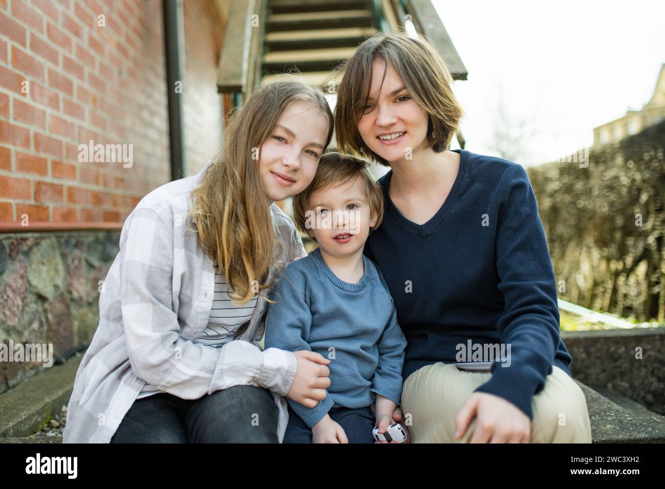 Cute big sisters cuddling with their toddler brother. Adorable teenage ...