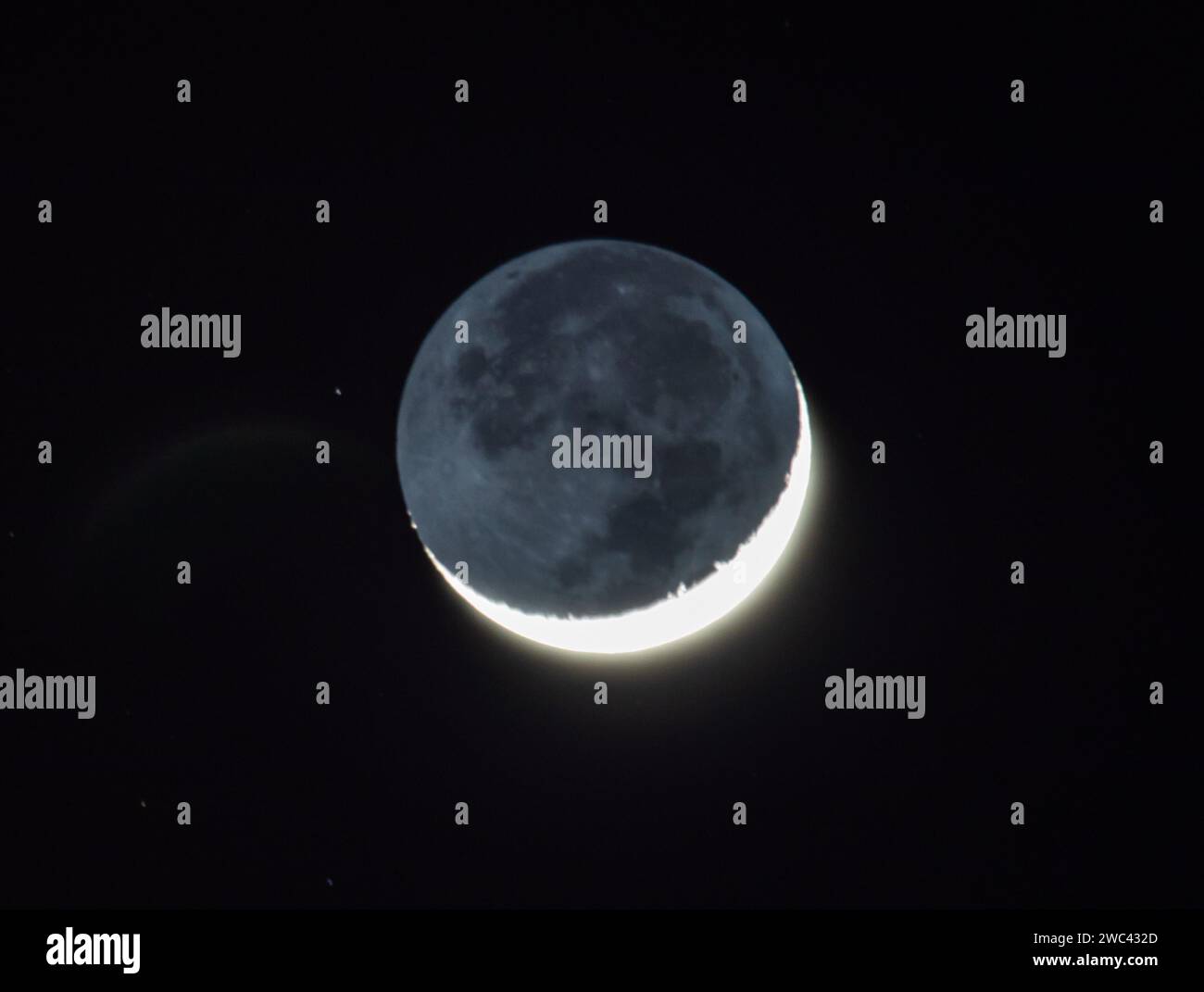 A crescent moon with shadow detail sinks slowly in a clear night sky on ...