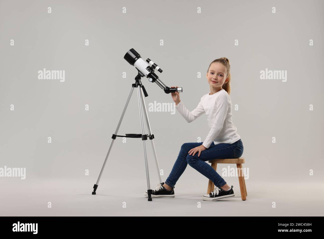 Happy little girl with telescope on light grey background Stock Photo ...