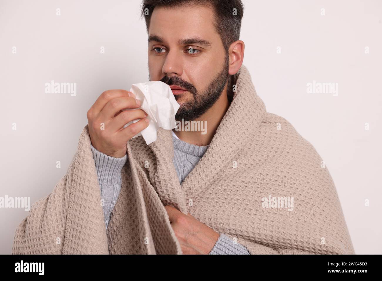 Sick man wrapped in blanket with tissue on light grey background. Cold ...