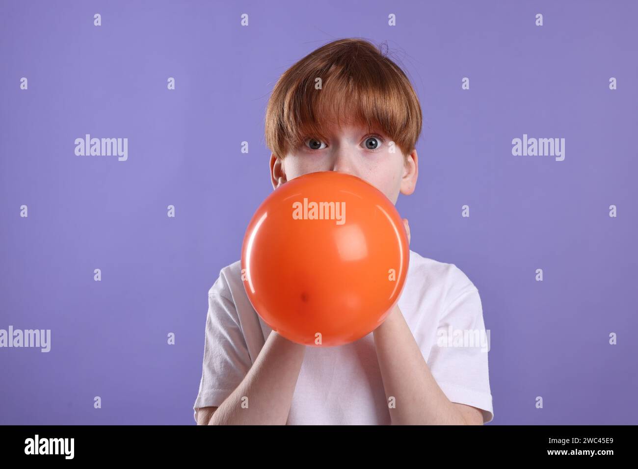 Boy inflating orange balloon on violet background Stock Photo - Alamy