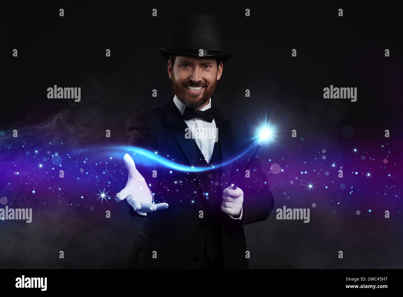 Smiling magician showing trick with wand on black background Stock ...