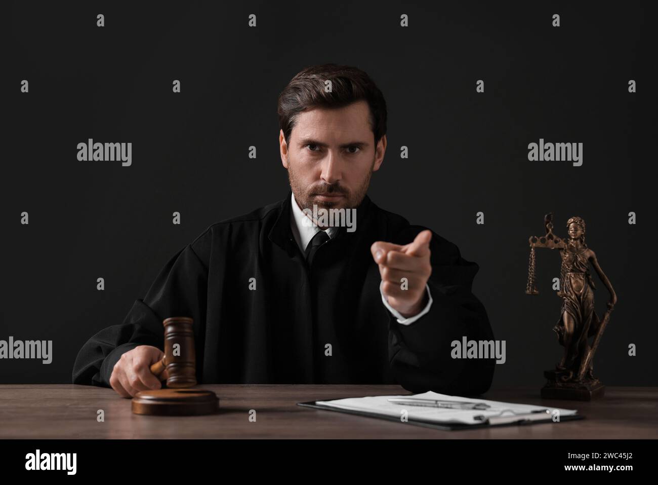 Judge with gavel pointing at wooden table against black background ...