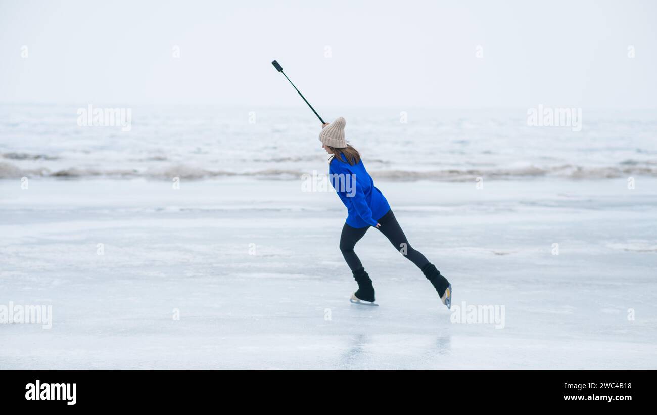 A caucasian woman is skating on a frozen lake holding a selfie stick in ...