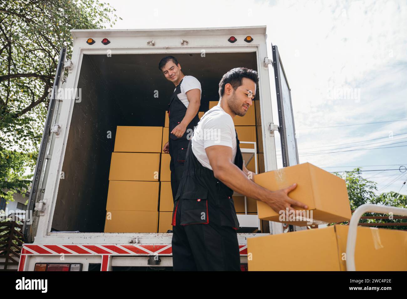 Delivery men unload boxes from a van. Movers in uniform work together ...