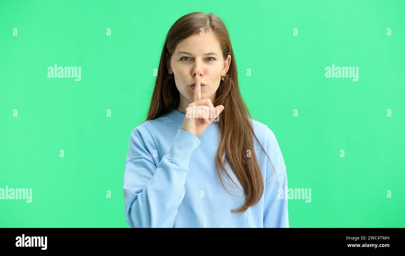 A woman, close-up, on a green background, shows a sign of silence Stock ...