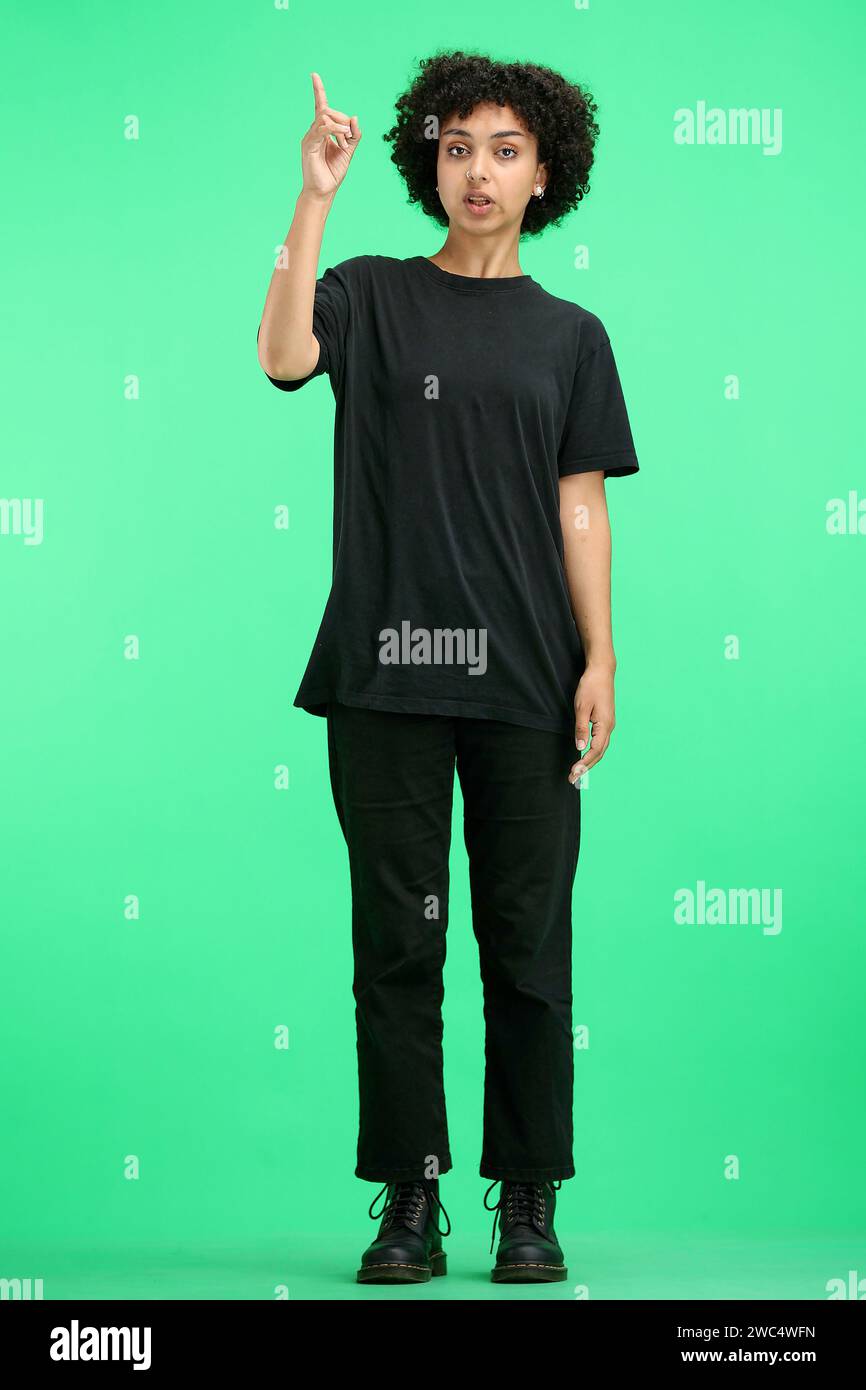 A woman, full-length, on a green background, shows an important sign ...