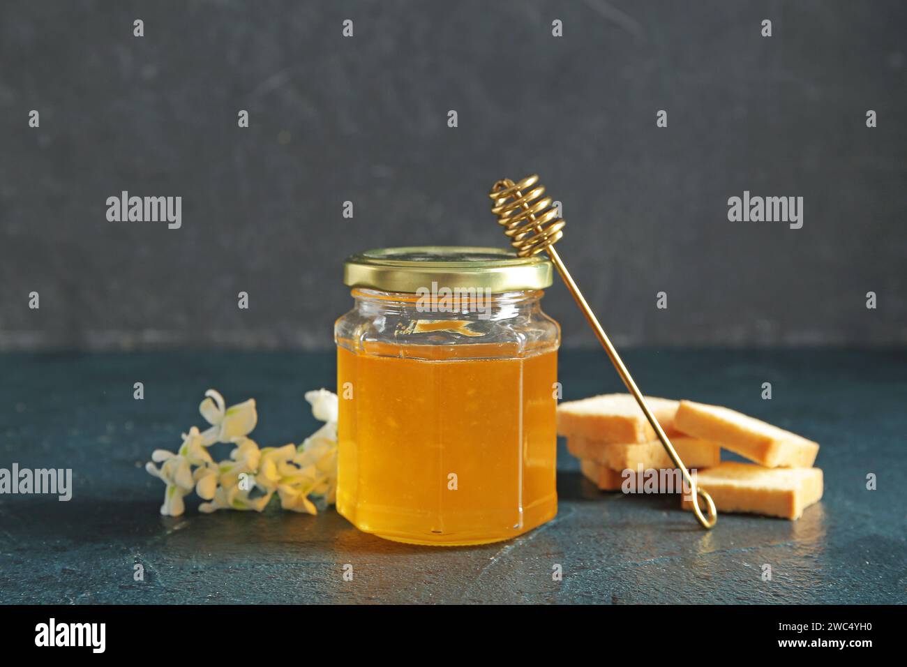 Jar of honey with flowers of acacia and crackers on dark background ...