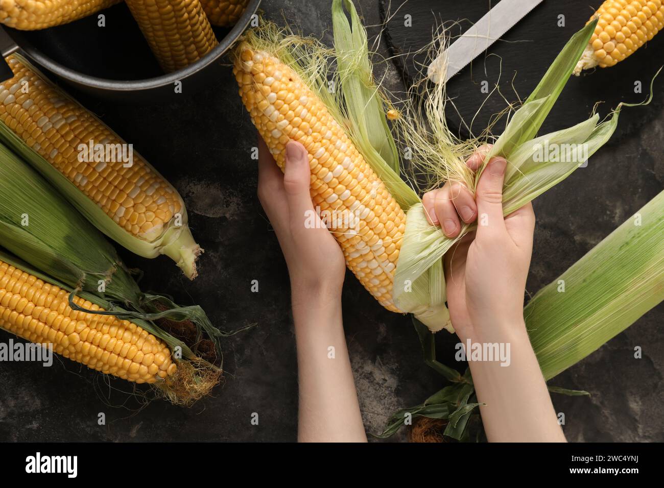 Woman peeling fresh corn cob on black background Stock Photo - Alamy