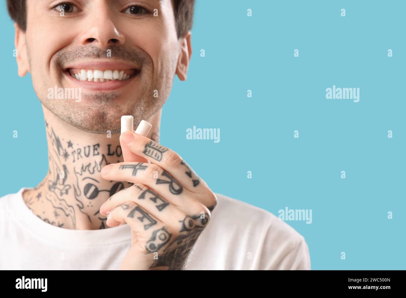 Young tattooed man with chewing gum on blue background, closeup Stock ...