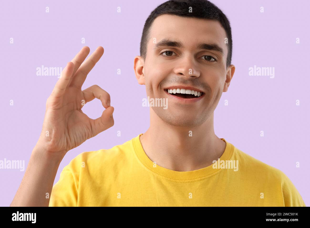 Handsome young man with healthy teeth showing OK gesture on purple ...