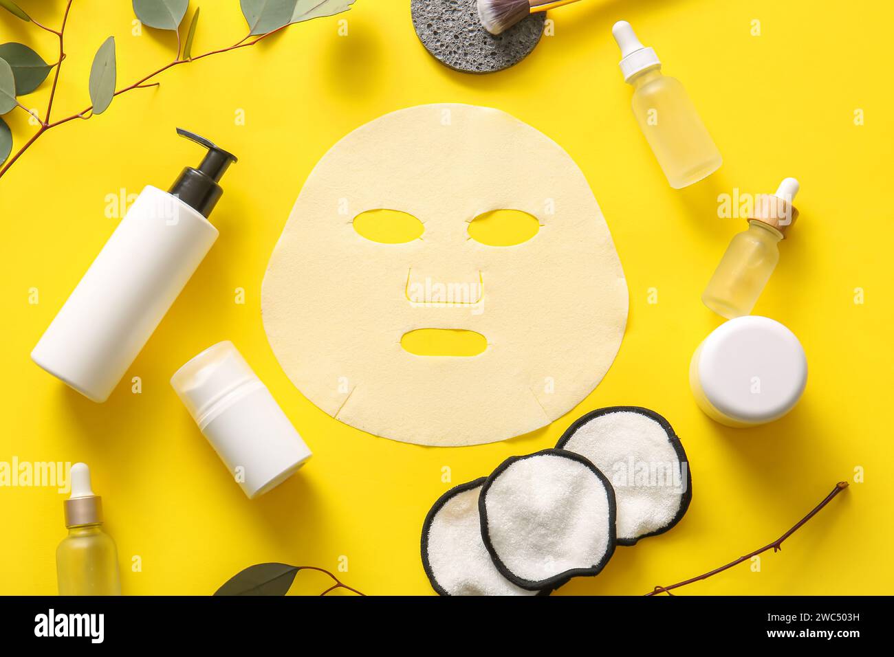 Facial sheet mask with different cosmetic products and leaves on yellow ...