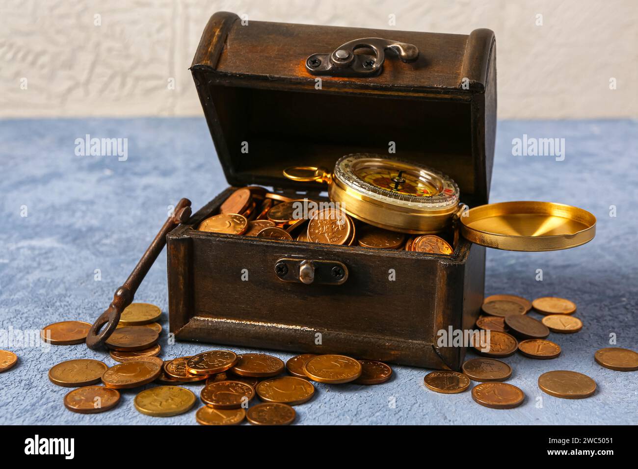 Old chest with coins, compass and key on blue grunge table near white ...