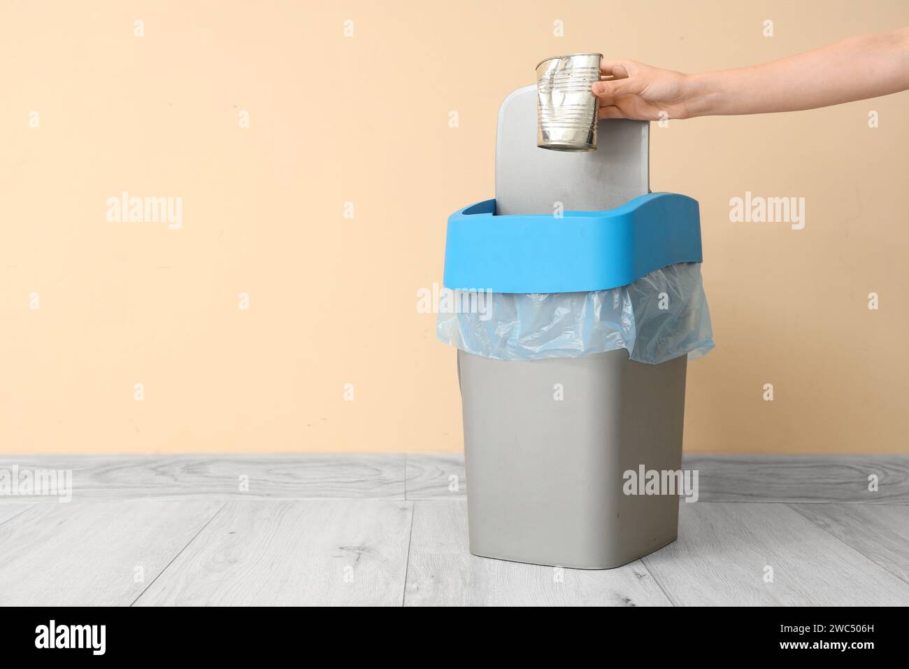 Female hand throwing can tin into trash bin near beige wall Stock Photo ...