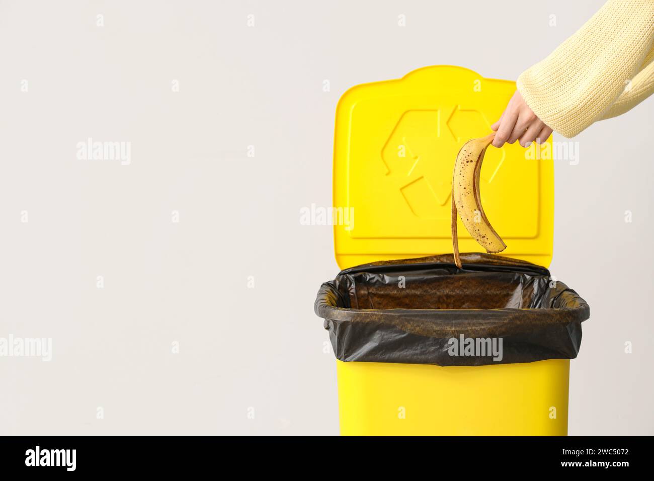 Woman throwing banana peel into trash bin near grey wall, closeup Stock ...