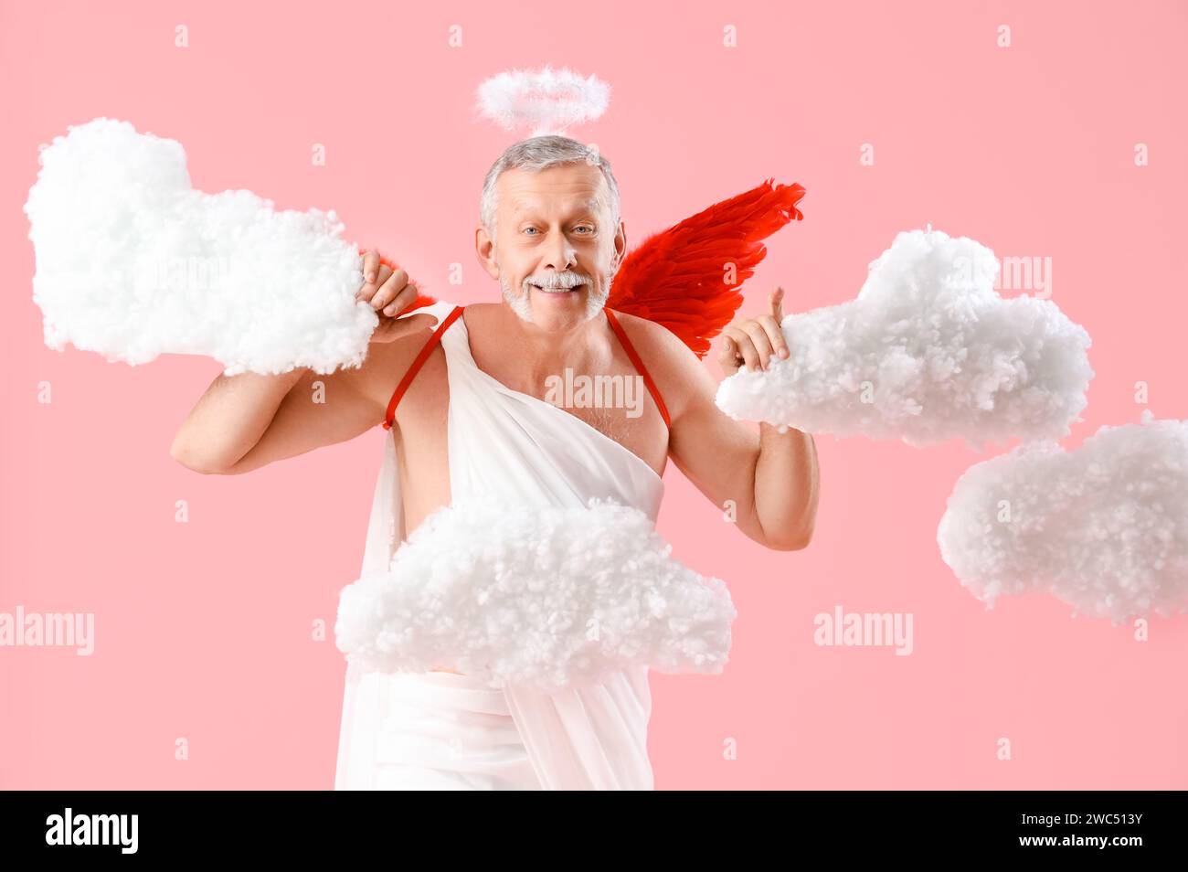 Mature man dressed as Cupid in clouds on pink background. Valentine's ...