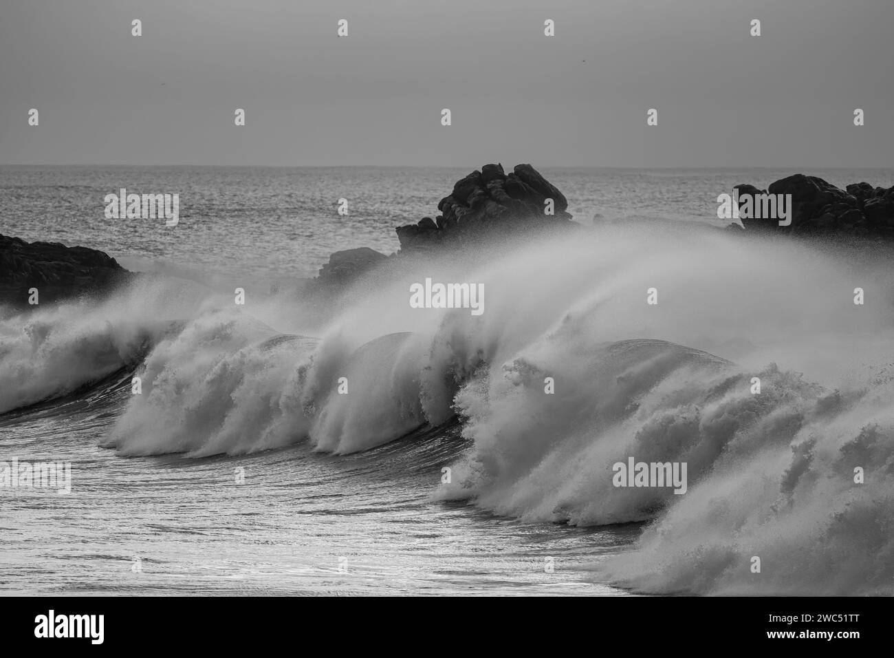 Black and white breaking stormy waves among rocks and cliffs with spray ...