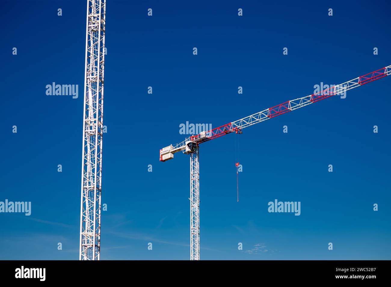Two construction tower cranes at a construction site against a blue sky ...
