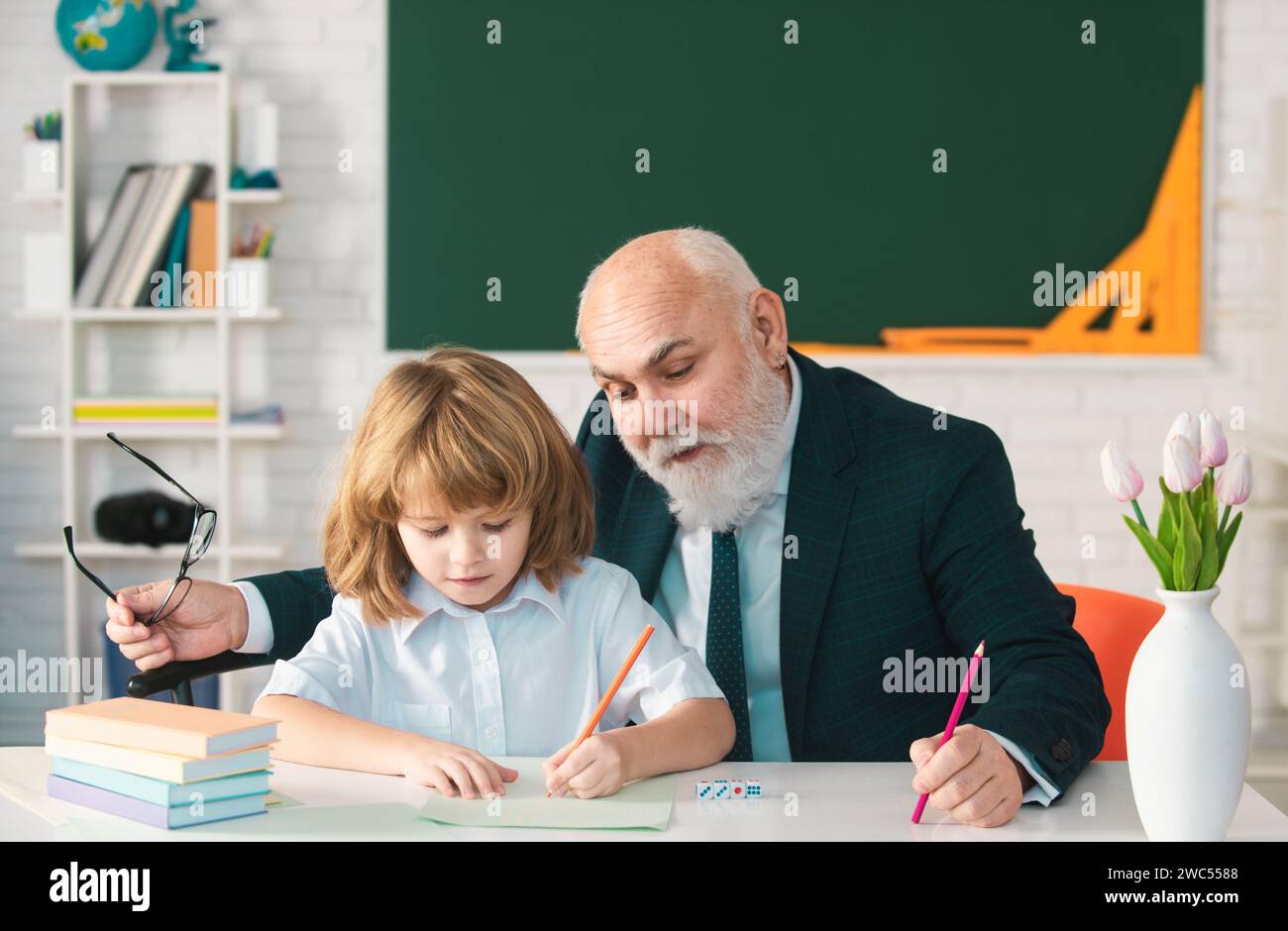 Old teacher and young schoolboy doing homework assignment at school ...