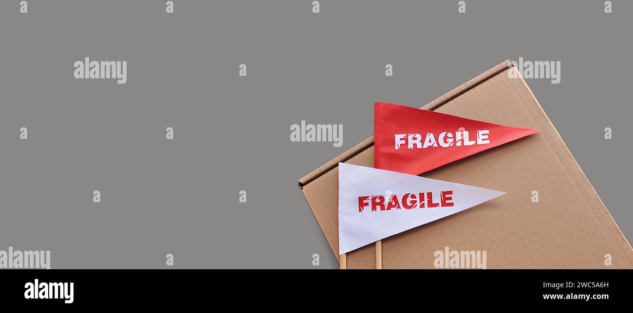 Small paper flags with the warning 'Fragile' as a label and empty cardboard box on monochrome ...