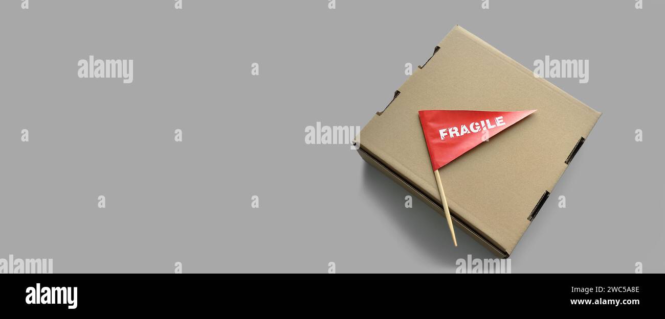 Small paper flags with the warning 'Fragile' as a label and empty cardboard box on monochrome ...