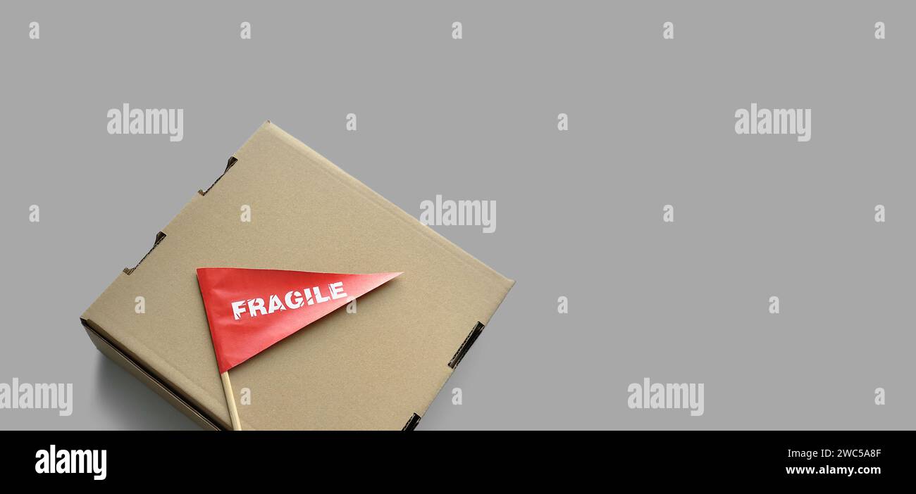 Small paper flags with the warning 'Fragile' as a label and empty cardboard box on monochrome ...