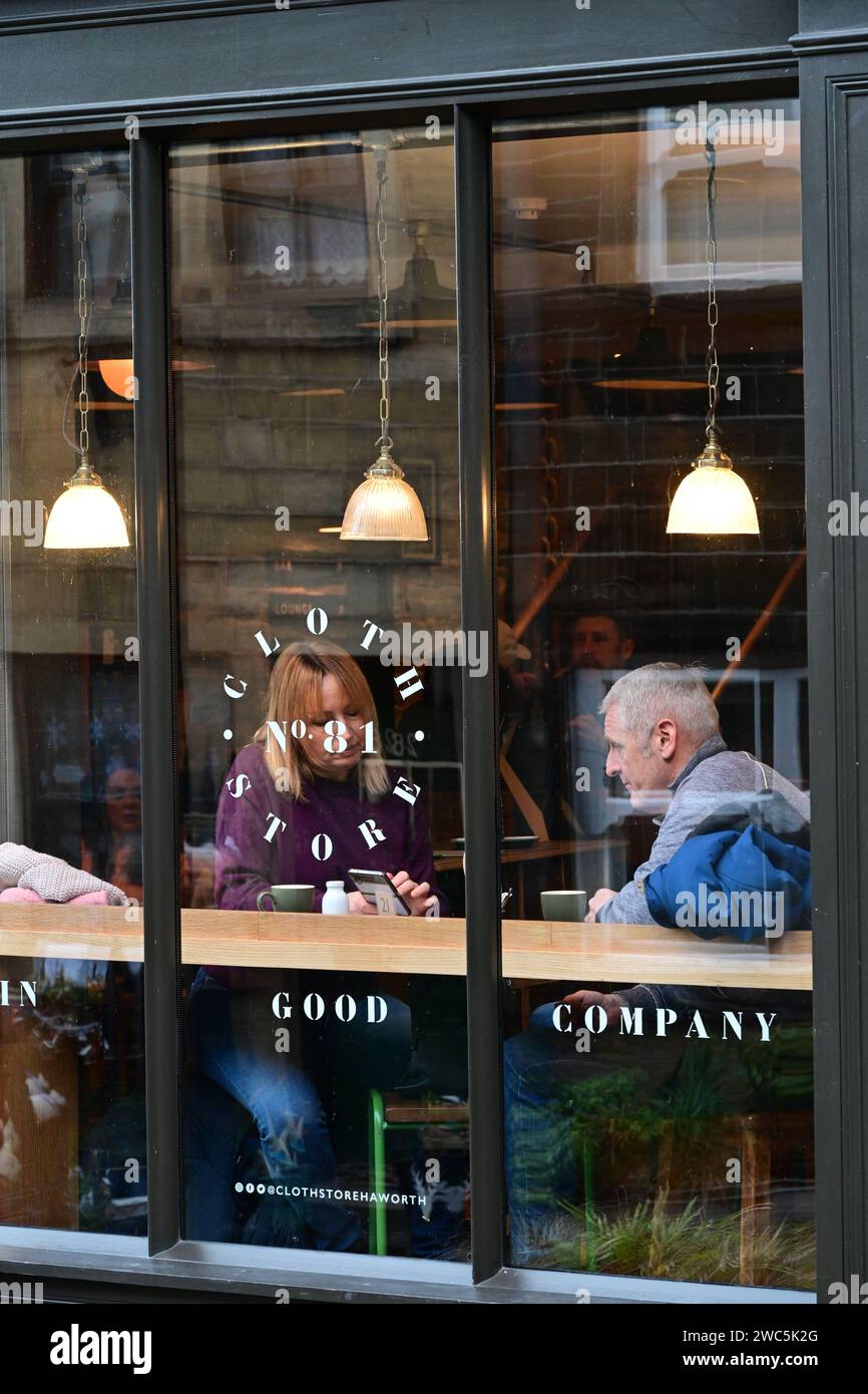 Two people sat in shop window, the cloth shop Haworth, West Yorkshire ...