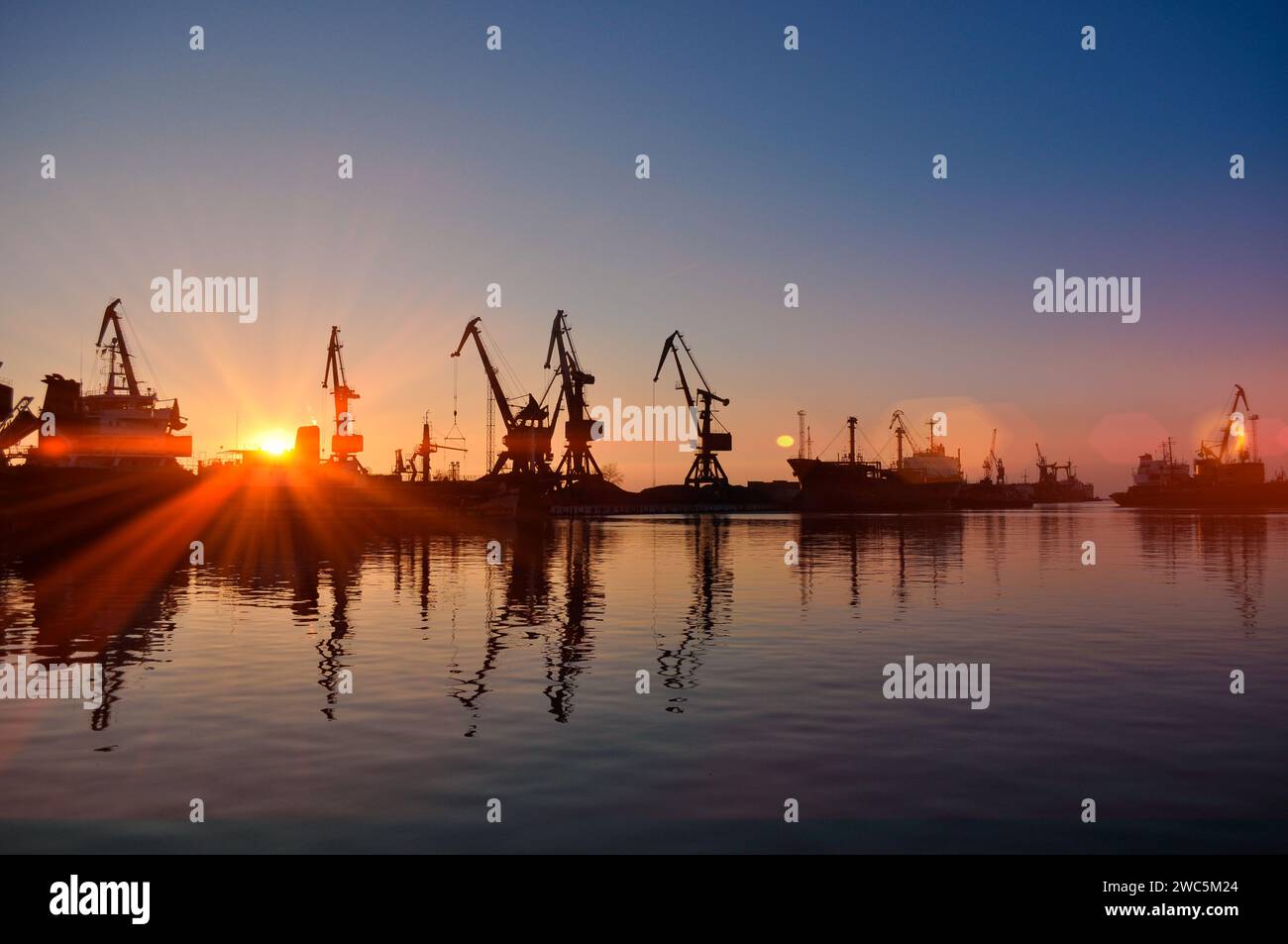 Sunset silhouettes shipping cranes at busy port. Commercial cargo docks ...