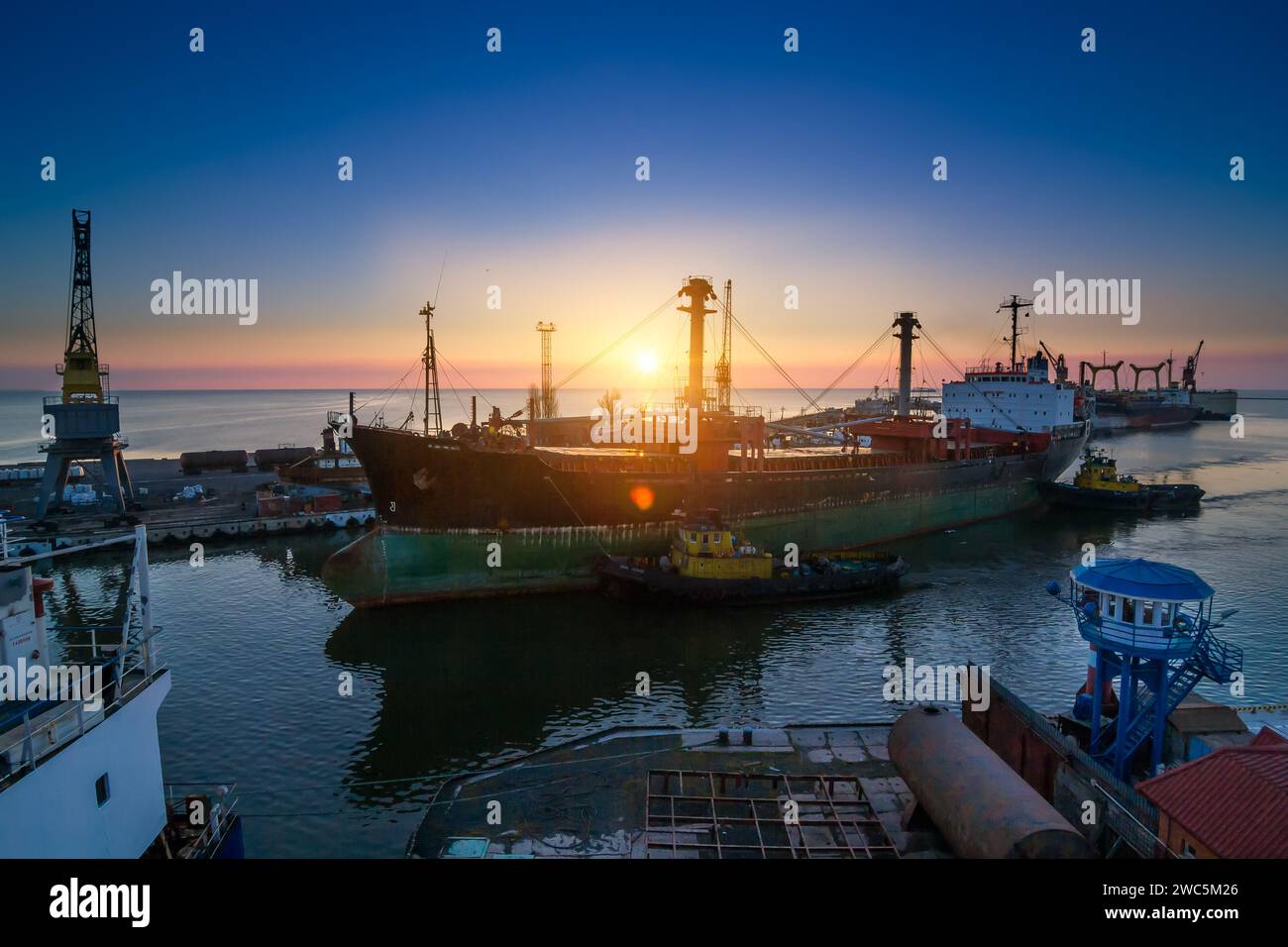 Commercial ships docked at sea port, sunrise backlighting vessels ...