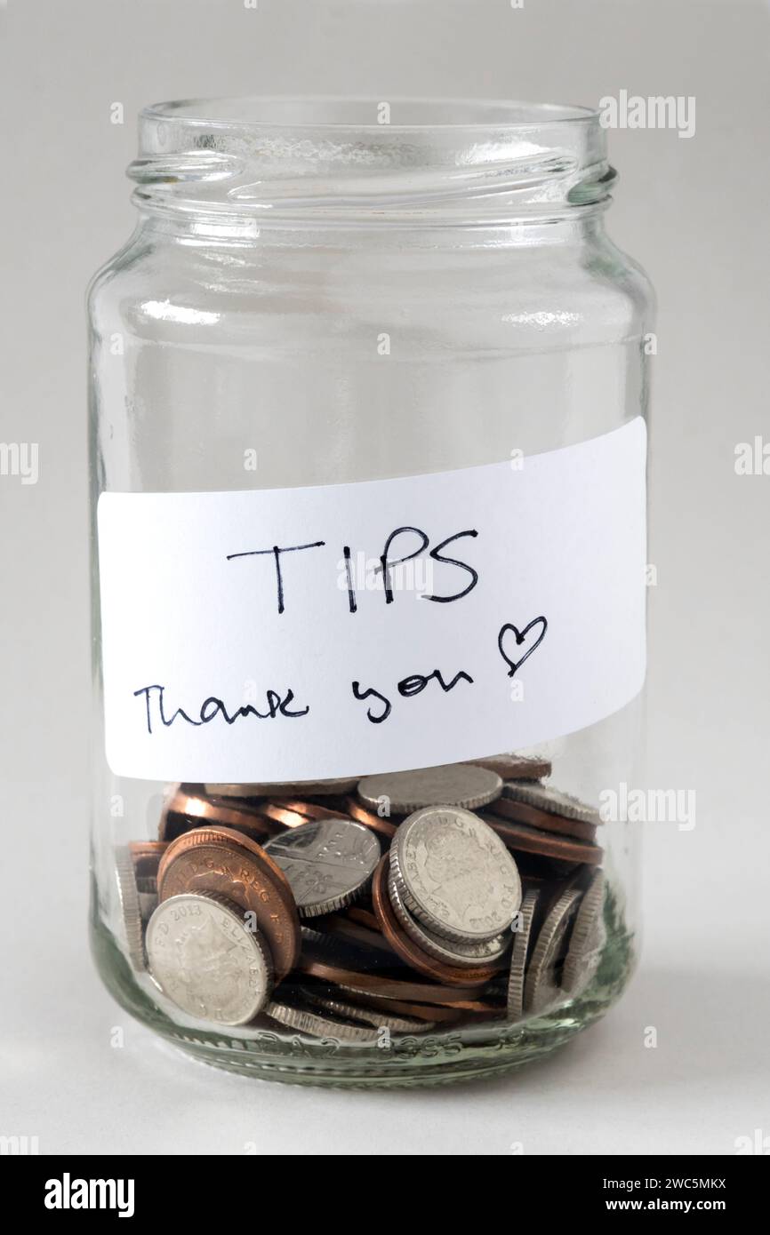 A tips jar containing money with a label reading Tips and Thank you ... A tips jar containing money with a label reading Tips and Thank you ...