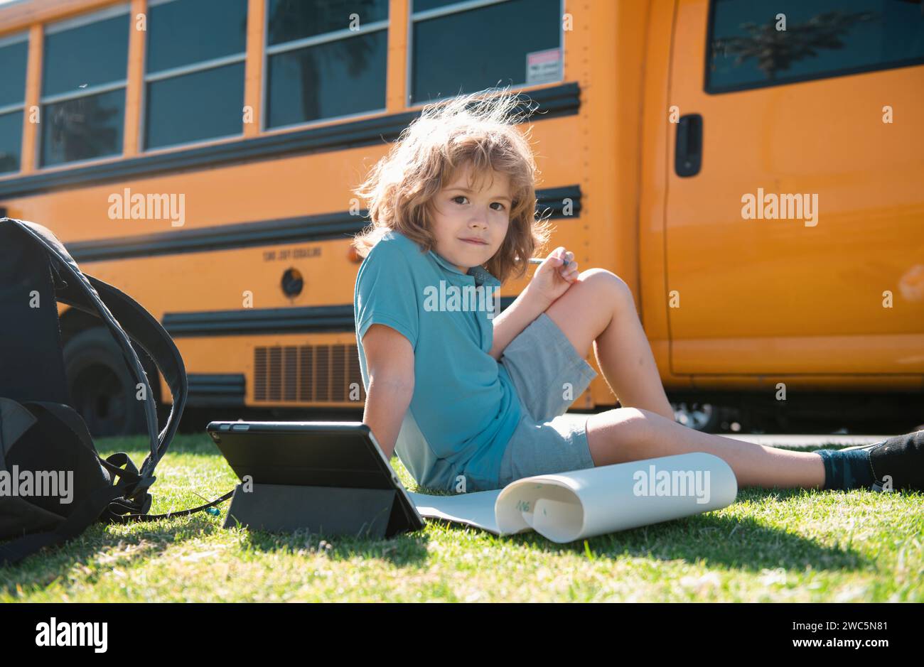 Pupil does school homework laying on grass in the park near school bus ...