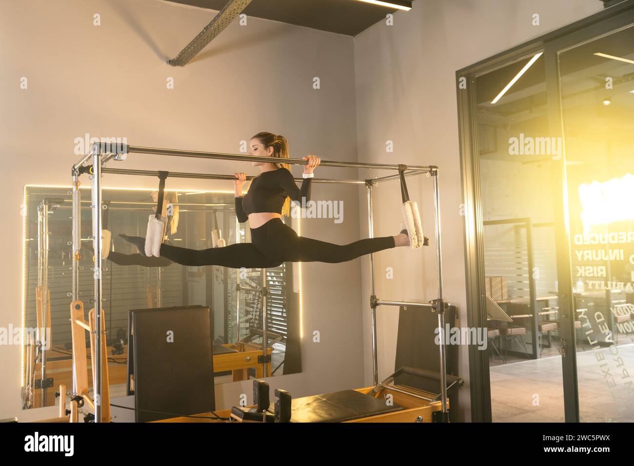 Woman performs an advanced flexibility exercise on a Pilates Reformer ...