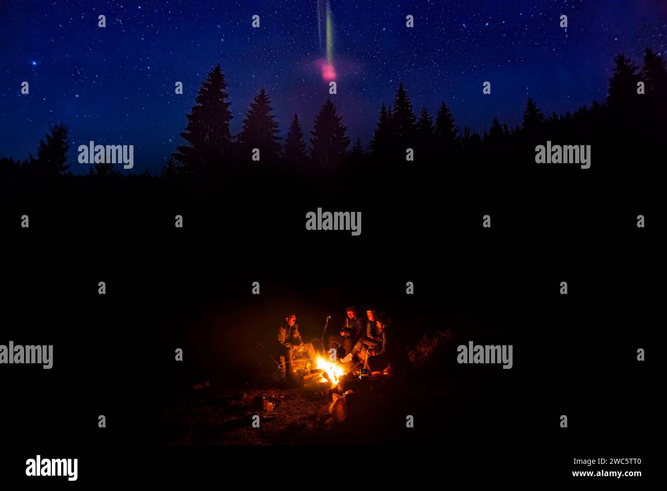 Group of people near the fireplace in the night forest with dark trees ...