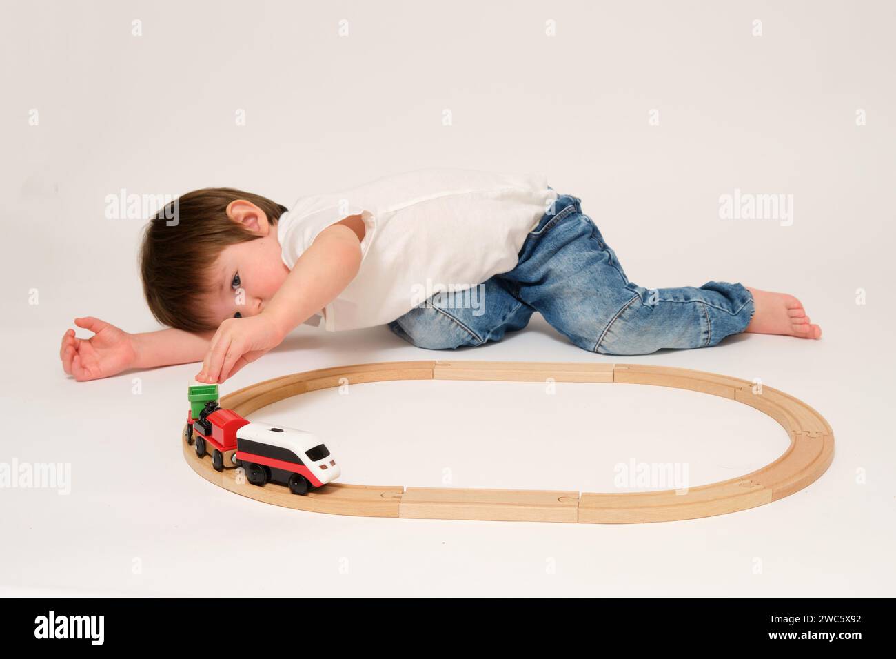 A child is playing train cars on the railway, studio white background ...