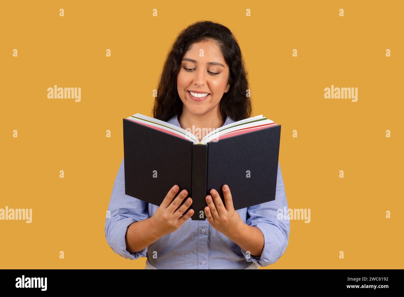 Content young woman with curly hair enjoying reading a book, showing a ...