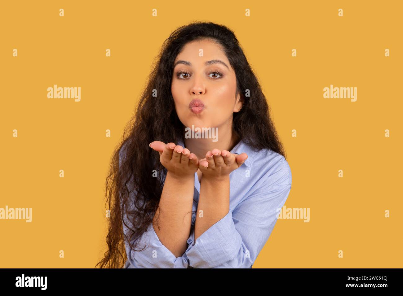 Charming young woman with long curly hair blowing a kiss, hands cupped ...