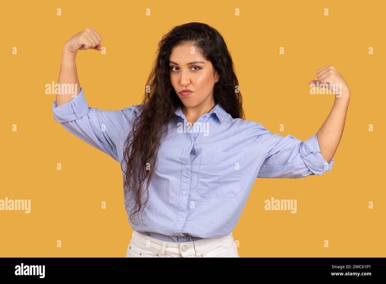 Strong, confident woman with wavy hair showing her muscles in a power ...