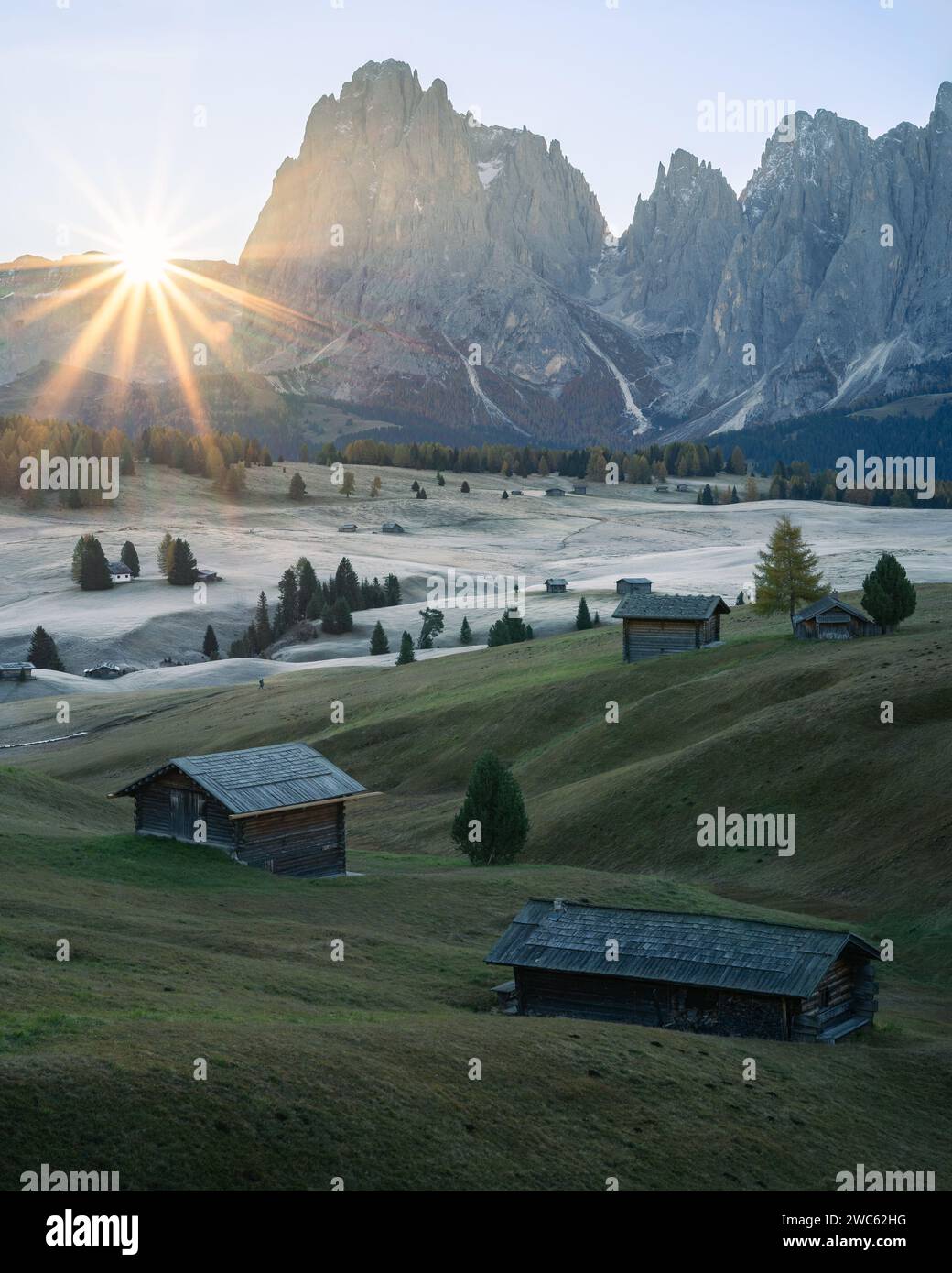 Vertical shot of Sun rising above high alpine pasture with cottages ...