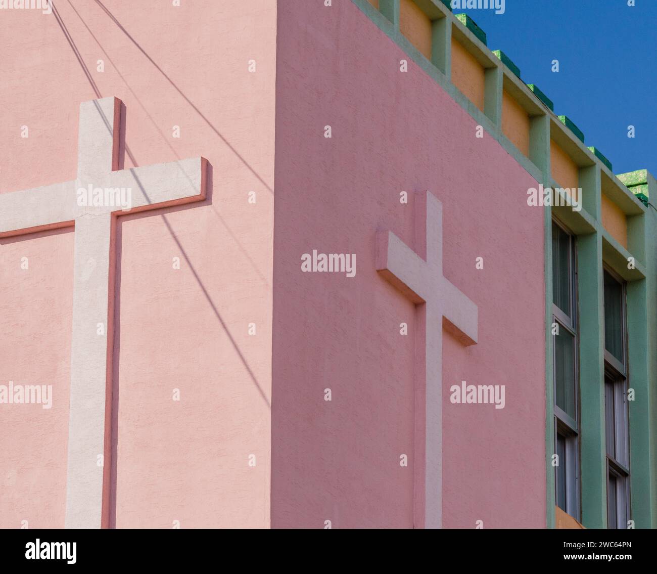 Crosses on side of a pink stucco building with power lines casting ...