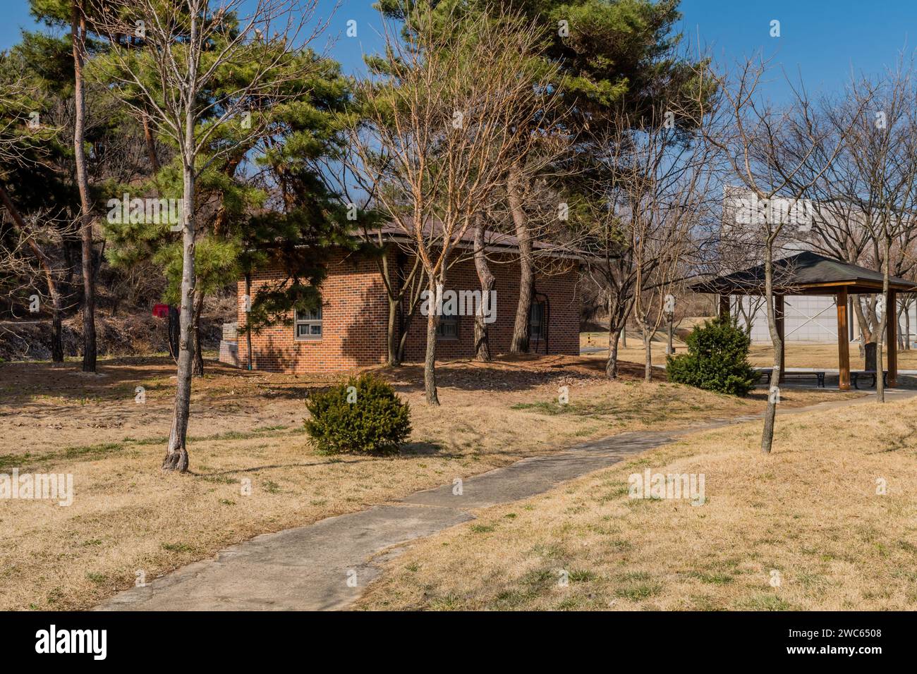 Red brick storage building under grove of trees next to covered park ...