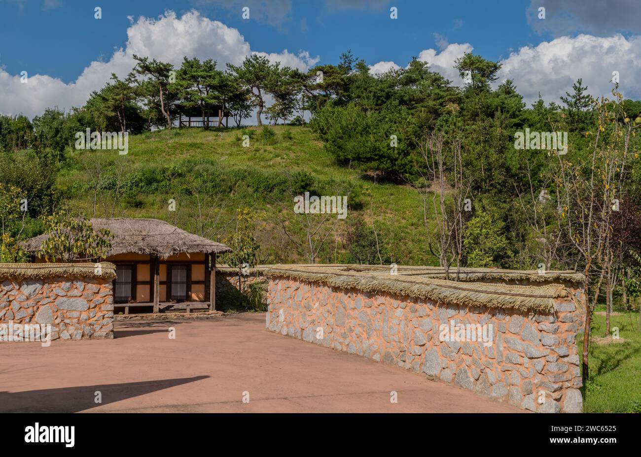 Old thatch roof building behind mud and stone wall at urban public park ...