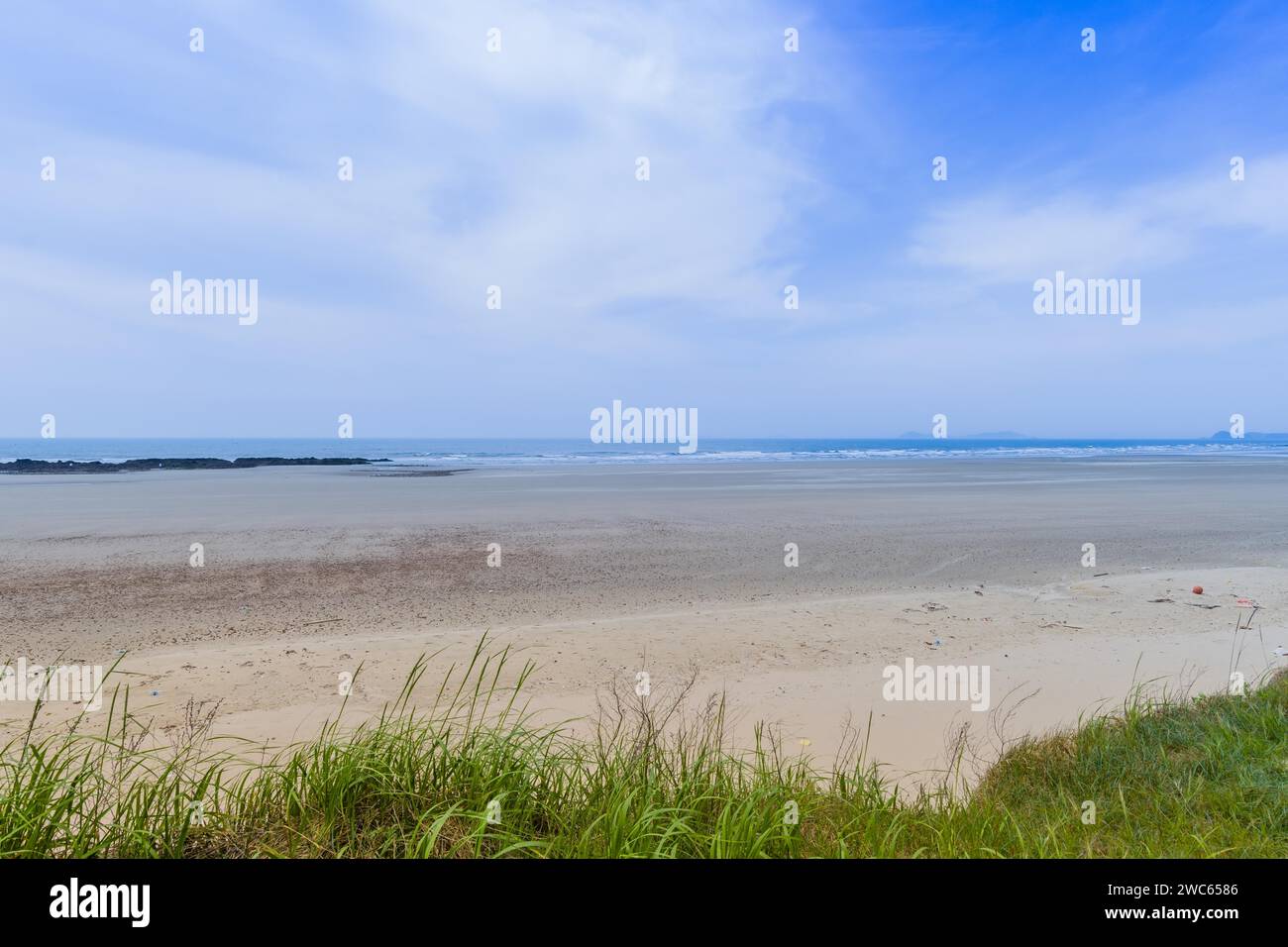 Landscape of sandy beach with rocky shore line under blue sky with ...