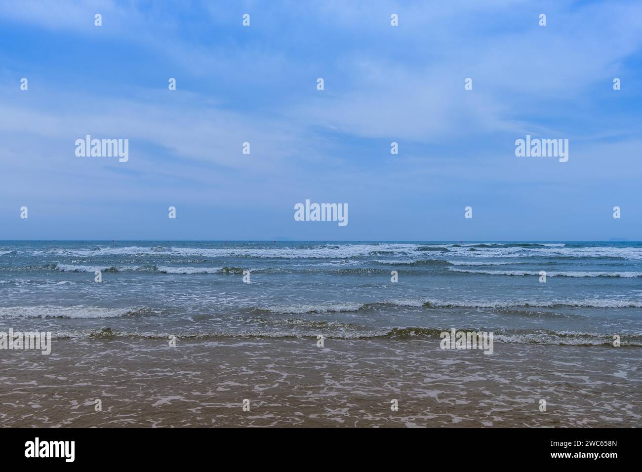 Rough ocean waves and white caps under a blue sky with low wispy cirrus ...