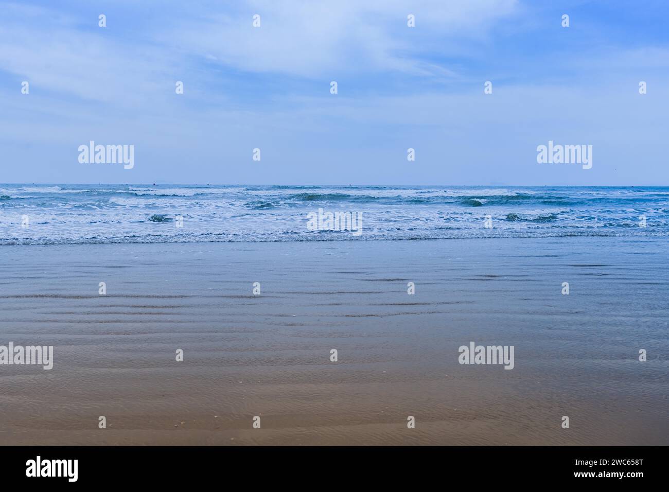 Sandy beach and rough ocean waves and white caps under a blue sky with ...
